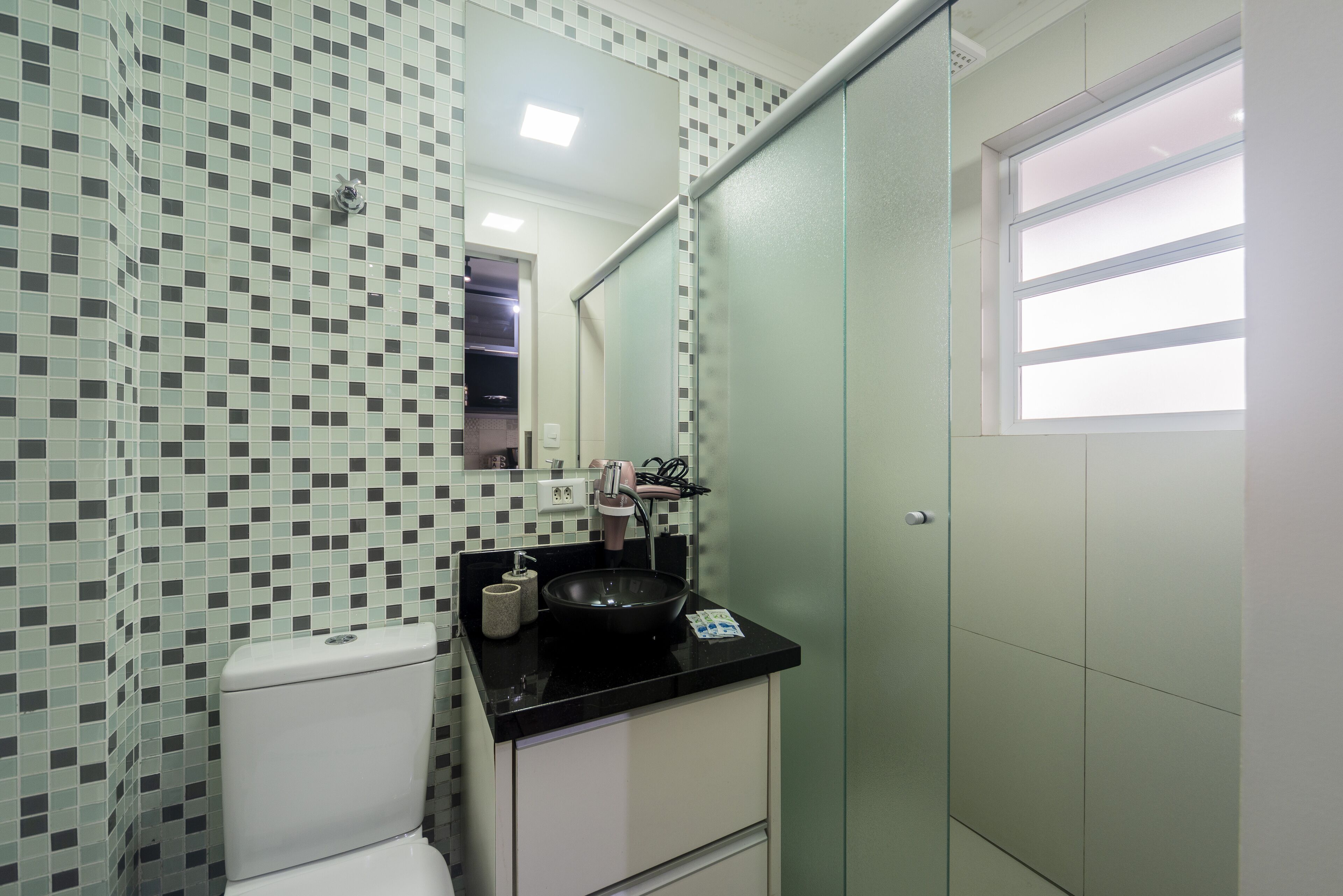 Casa de banho com painel de azulejos, lavatório preto, sanita e espelho.