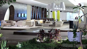 Um hall de hotel moderno com áreas de estar, balcão de recepção e uma planta grande em primeiro plano.