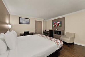 Quarto de hotel com cama, escrivaninha, televisão e uma cadeira.