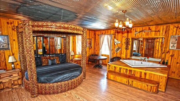 Quarto em estilo de cabana de tronco com uma cama de dossel, um banco de madeira, uma pia e um espelho.