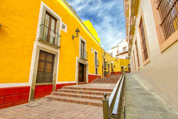 Uma rua estreita com edifícios amarelos, uma escadaria e um corrimão de metal.
