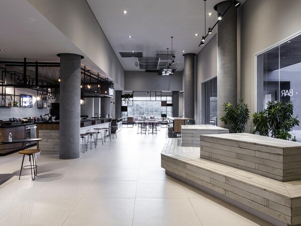 Um espaço de bar amplo, com pé-direito alto, iluminação moderna e vista para o exterior.