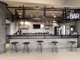 Uma área de bar moderna com balcão, banquetas e um letreiro que diz 'BAR'.