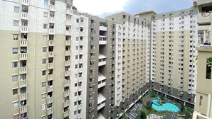 Um edifício residencial alto com várias varandas, um pátio central com piscina e antenas parabólicas nos terraços.