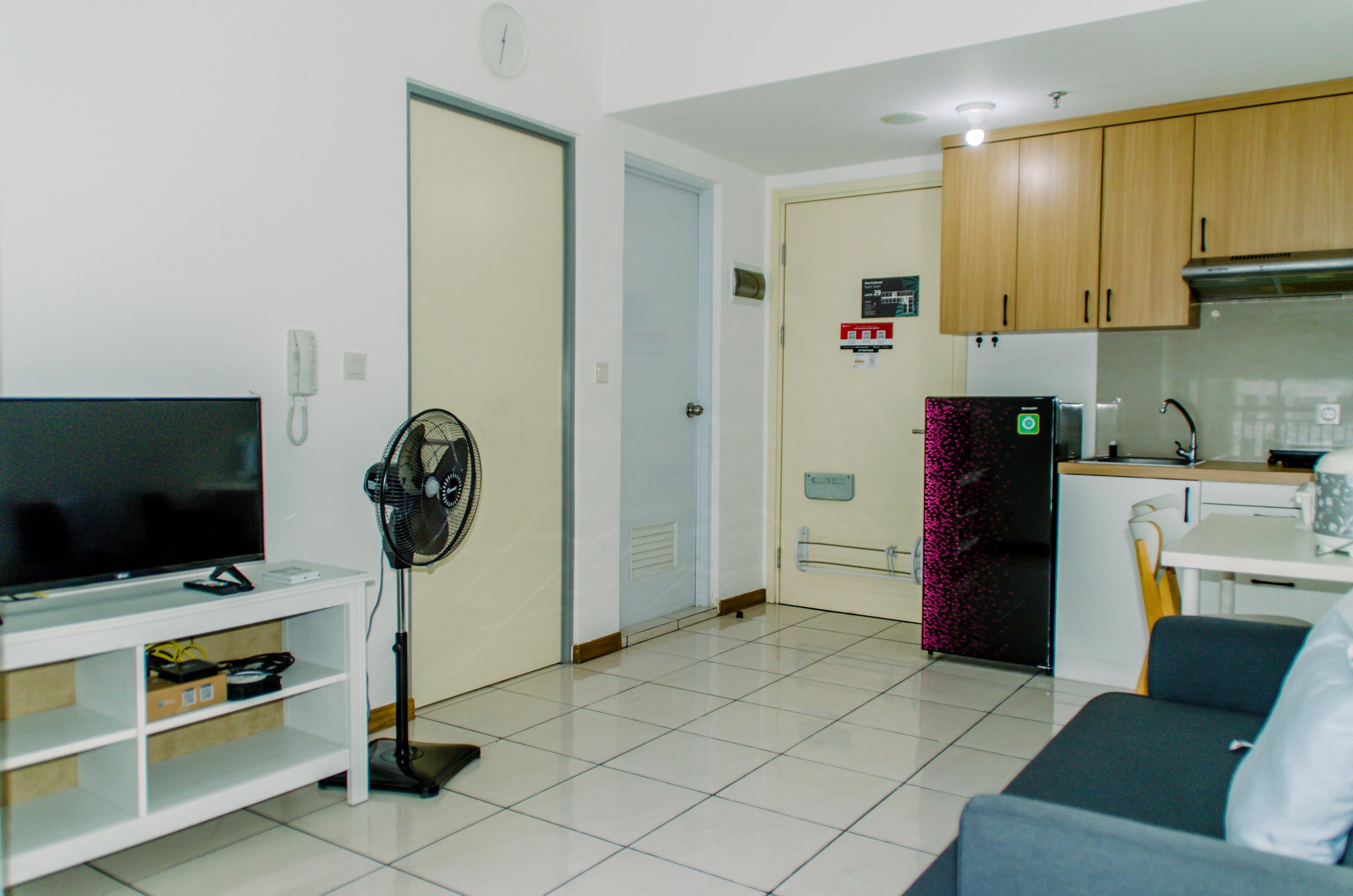 Sala de estar com TV, ventoinha e sofá. Cozinha com arm ários e geladeira.
