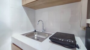 Uma cozinha com pia de aço inoxidável, fogão por indução preto e paredes com azulejos brancos.