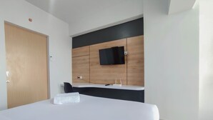 Quarto de hotel com cama, parede revestida de madeira, televisão montada e escrivaninha com cadeira.