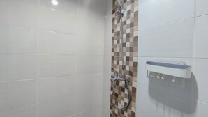 Casa de banho com azulejos brancos, chuveiro com padrão xadrez e lavatório branco com saboneteira.