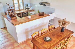 Uma cozinha com uma ilha de madeira, uma mesa de jantar com cadeiras e uma planta em vaso na ilha.
