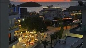 Área de piscina no terraço, com vista para o pôr do sol sobre o mar, cercada por edifícios.