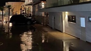 Um edifício de vários andares com varandas, chão molhado e um carro estacionado.