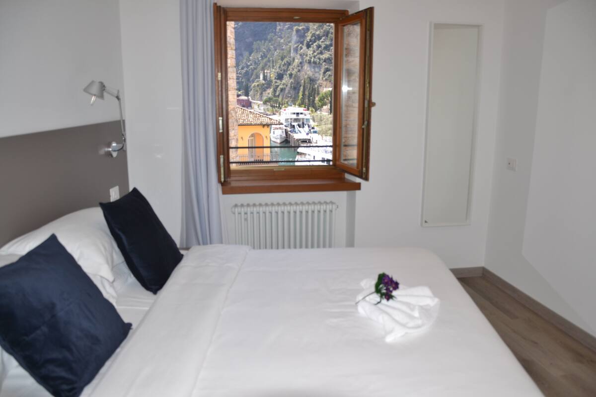 Quarto de hotel com cama, janela com vista para barcos e uma montanha, e um radiador.