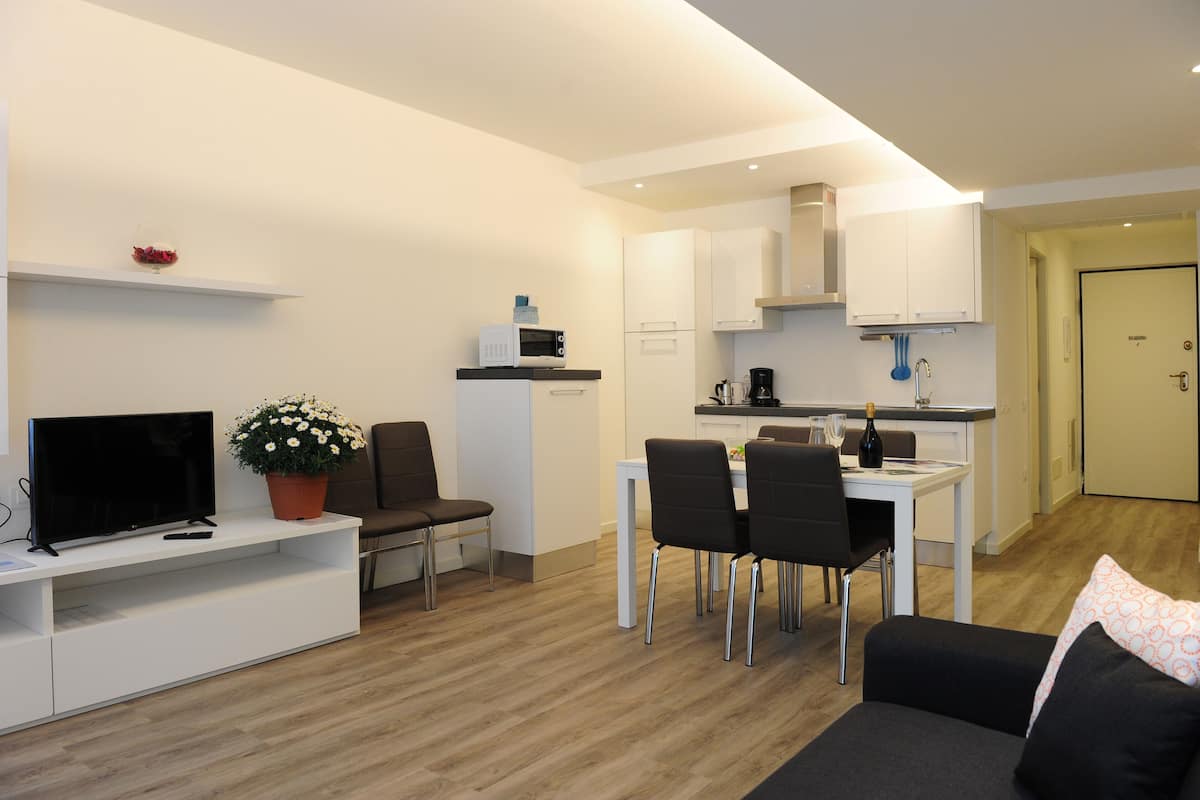 Uma sala de estar moderna com uma televisão de tela plana, um sofá e uma área de jantar com mesa e cadeiras.