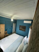 Quarto com cama, guarda-roupa de madeira, radiador, porta branca e ventoinha no teto.