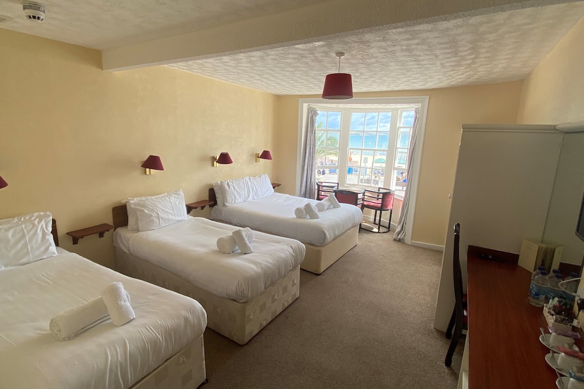 Quarto de hotel com duas camas, uma mesinha e vista para a praia.
