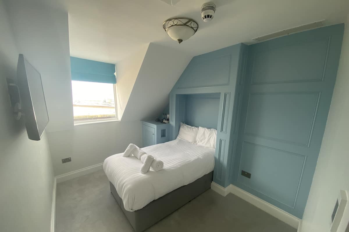 Um quarto com cama, mesa de cabeceira, cômoda, janela e porta.