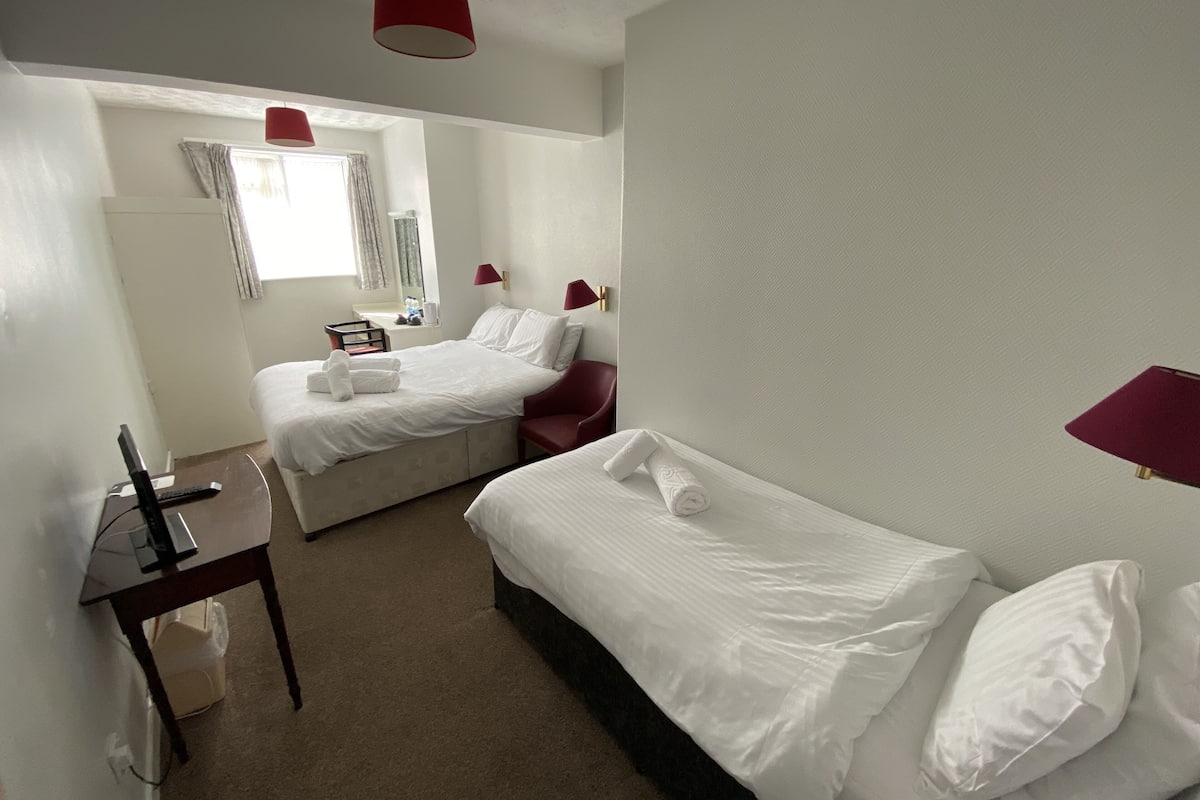 Quarto de hotel com duas camas, uma mesa e uma cadeira.