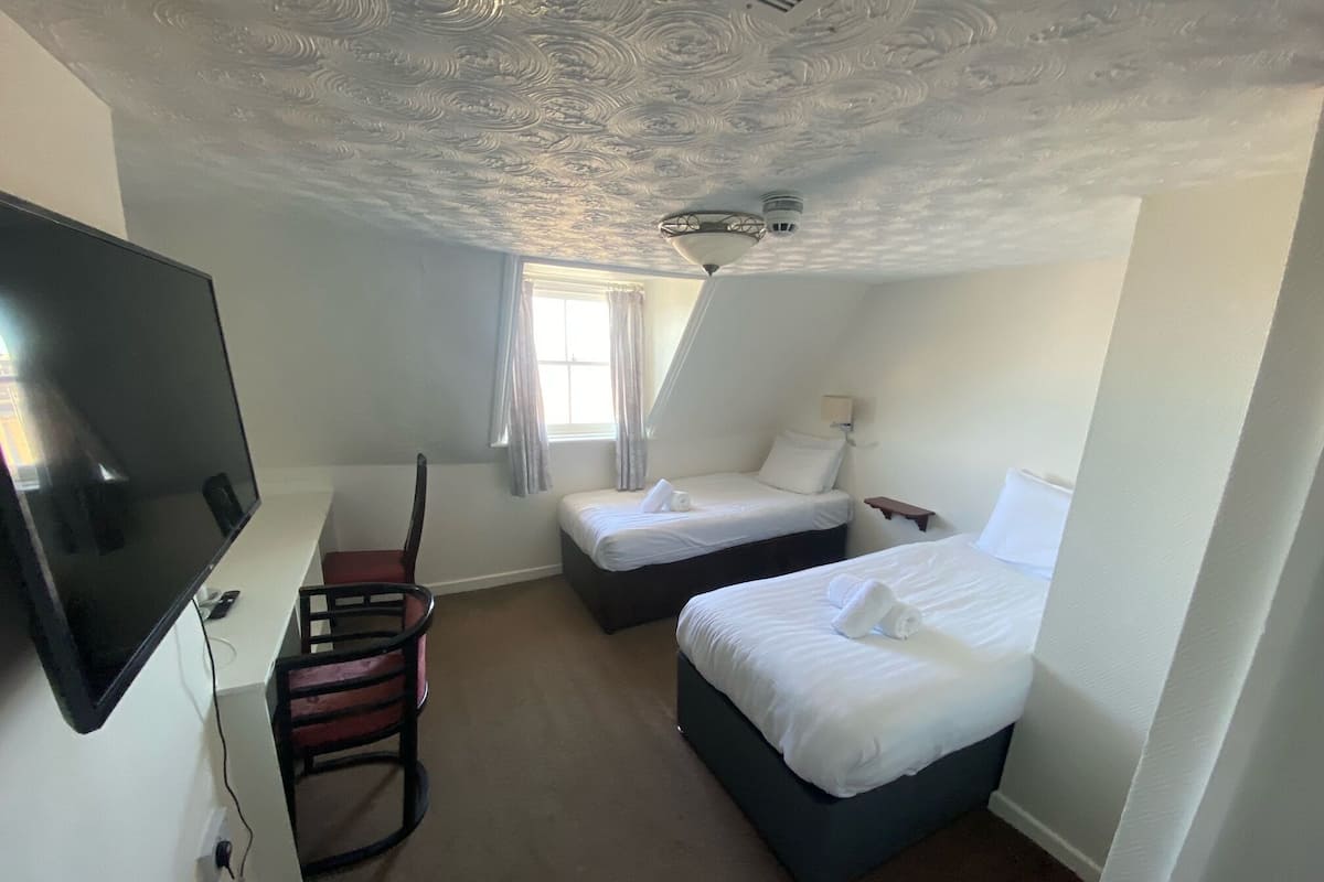 Quarto com duas camas, televisão, cadeira e janela com cortinas.