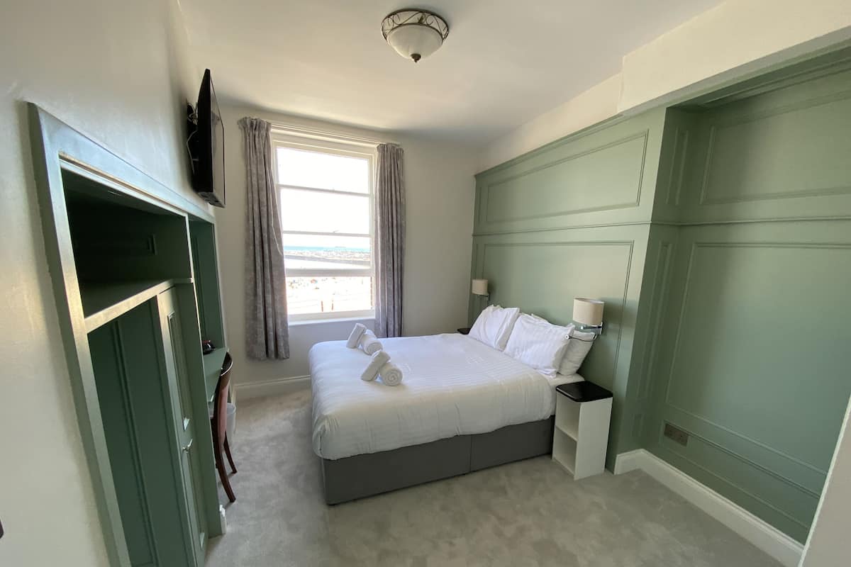 Quarto com cama, mesa de cabeceira, televisão, janela com cortinas e parede verde.