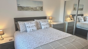 Quarto bem arrumado com uma cama grande, duas mesas de cabeceira com abajures, cômoda e um espelho.