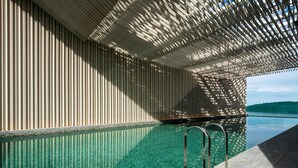 Piscina interna com vista clara da água, emoldurada por um design arquitetônico moderno com ripas verticais de madeira e barreira de vidro.