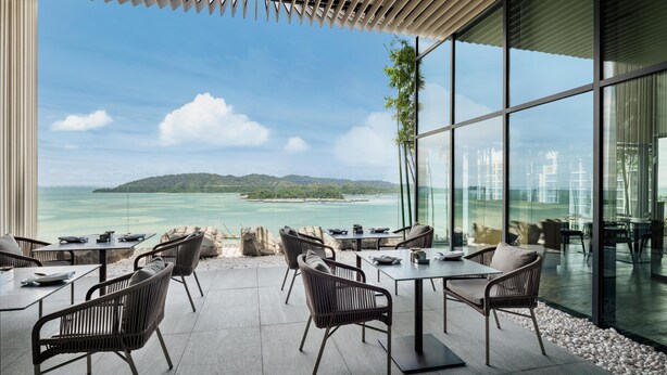 Terraço com mesas e cadeiras, vista para um corpo d'água e uma ilha ao longe.