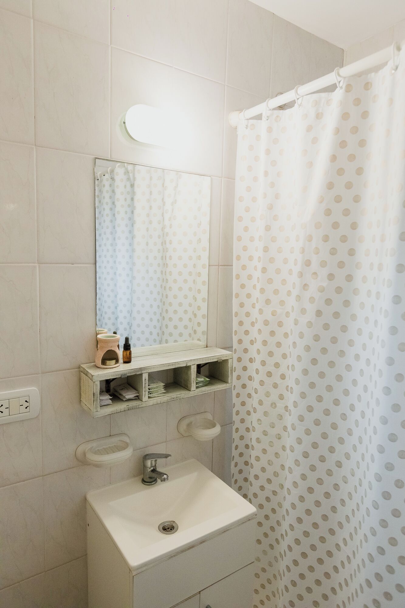 Uma casa de banho com uma pia branca, um espelho e uma cortina de chuveiro com padrão de bolinhas.