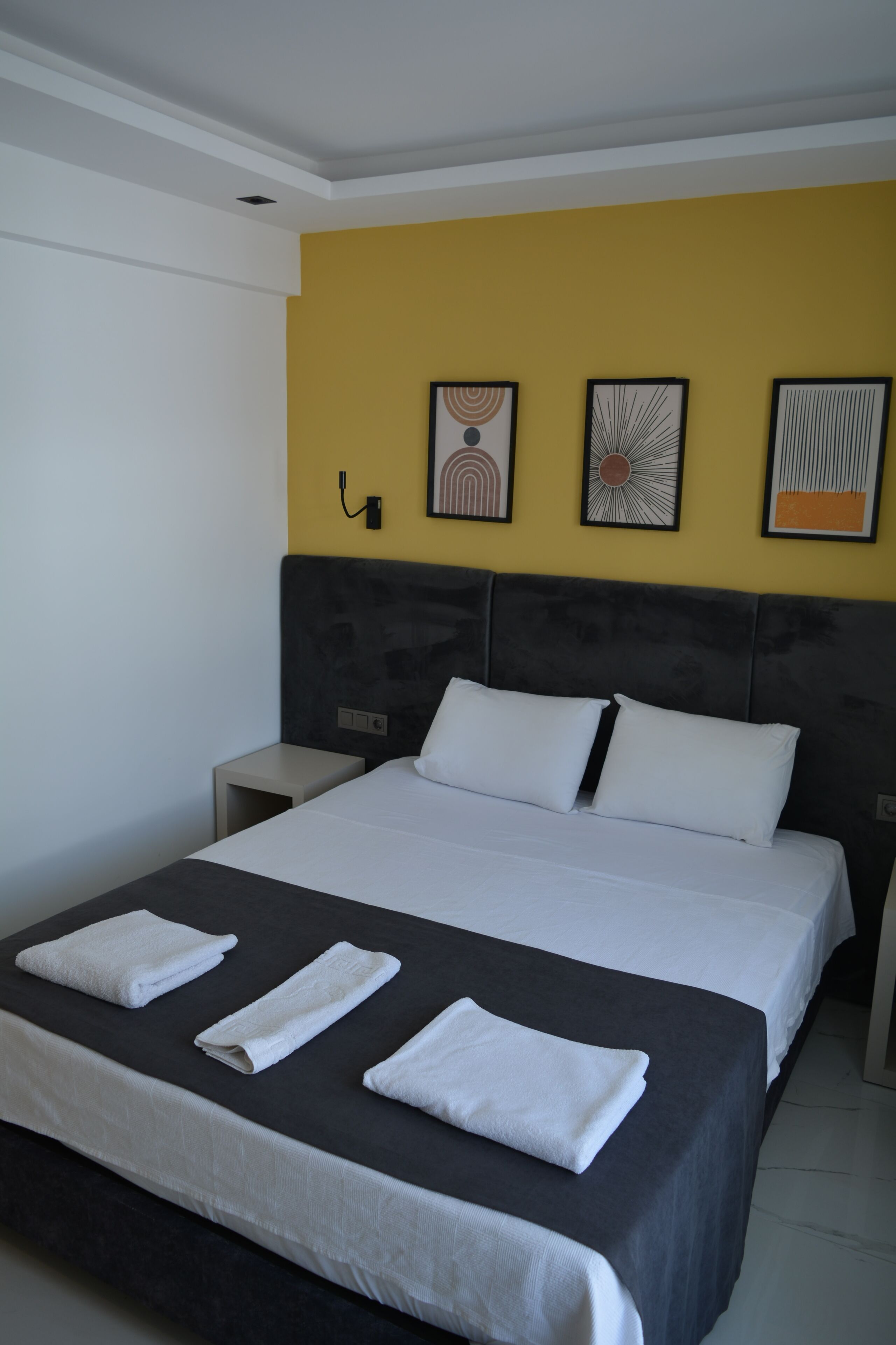 Quarto de hotel moderno com uma cama grande, uma mesinha de cabeceira e uma tomada na parede.