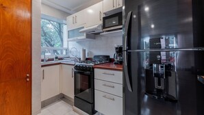 Uma cozinha moderna com armários brancos, uma geladeira preta, micro-ondas, fogão e cafeteira.