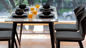 Uma mesa de jantar posta com tigelas e copos pretos, um lustre pendurado e vista para árvores pela janela.