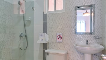 Um banheiro com chuveiro em box de vidro, vaso sanitário e pia.