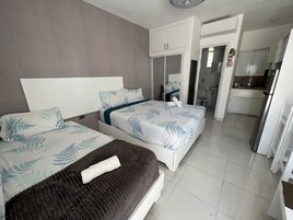 Quarto de hotel com duas camas, banheiro e cozinha compacta.