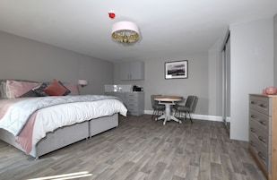 Quarto moderno com cama, mesa de cabeceira e um pequeno espaço de refeições com mesa e cadeiras.