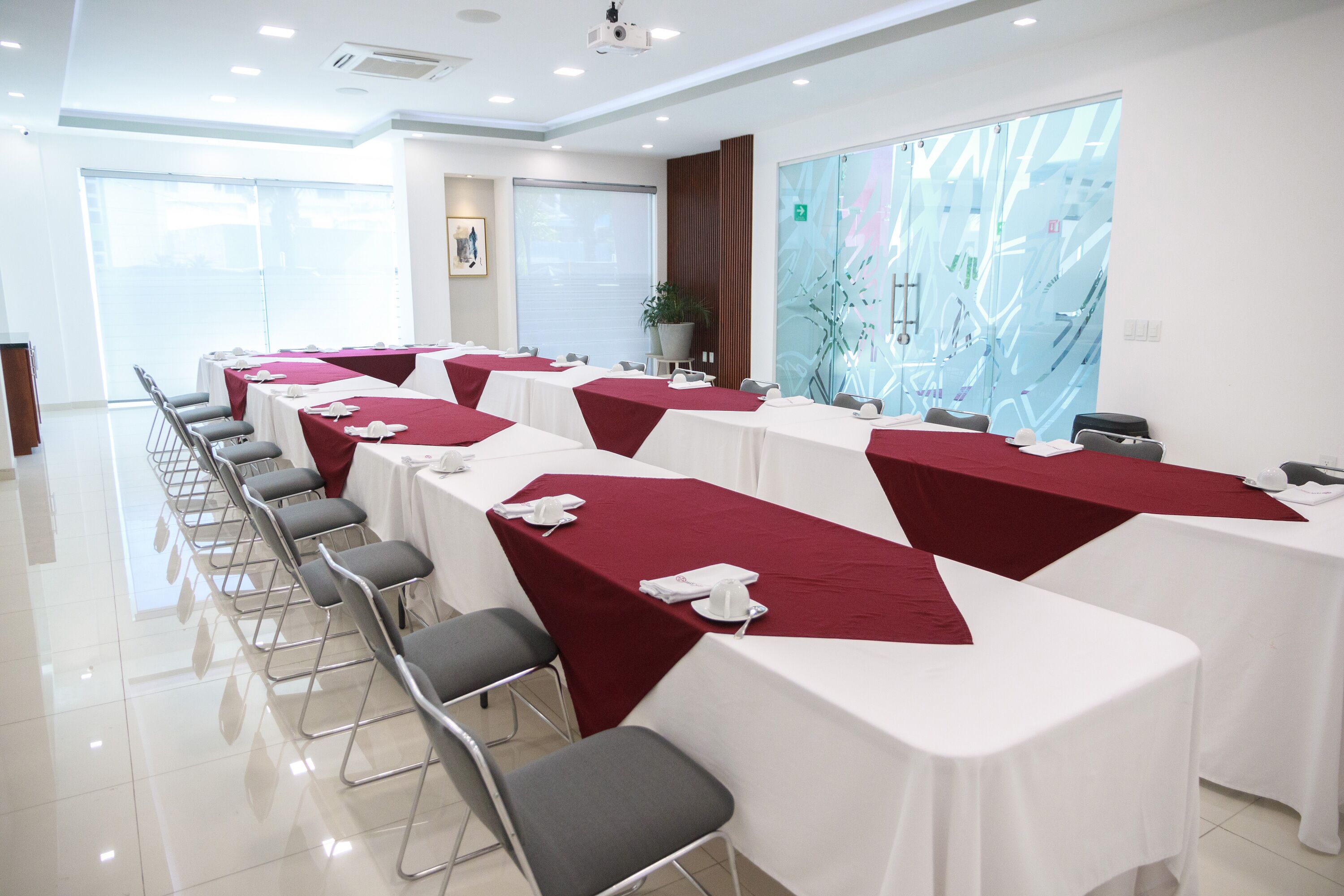 Uma sala de conferências com várias mesas e cadeiras, janelas amplas e um projetor.