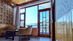 Quarto com teto de madeira, uma grande janela com vista para uma colina arborizada, painel de parede em madeira e uma poltrona bege.