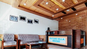 Uma área de recepção com um balcão de madeira identificado como "NATURE VILLA RESORT", um sofá confortável e uma mesa de centro.