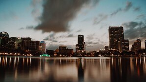 Paisagem urbana noturna com arranha-céus refletidos em águas calmas.