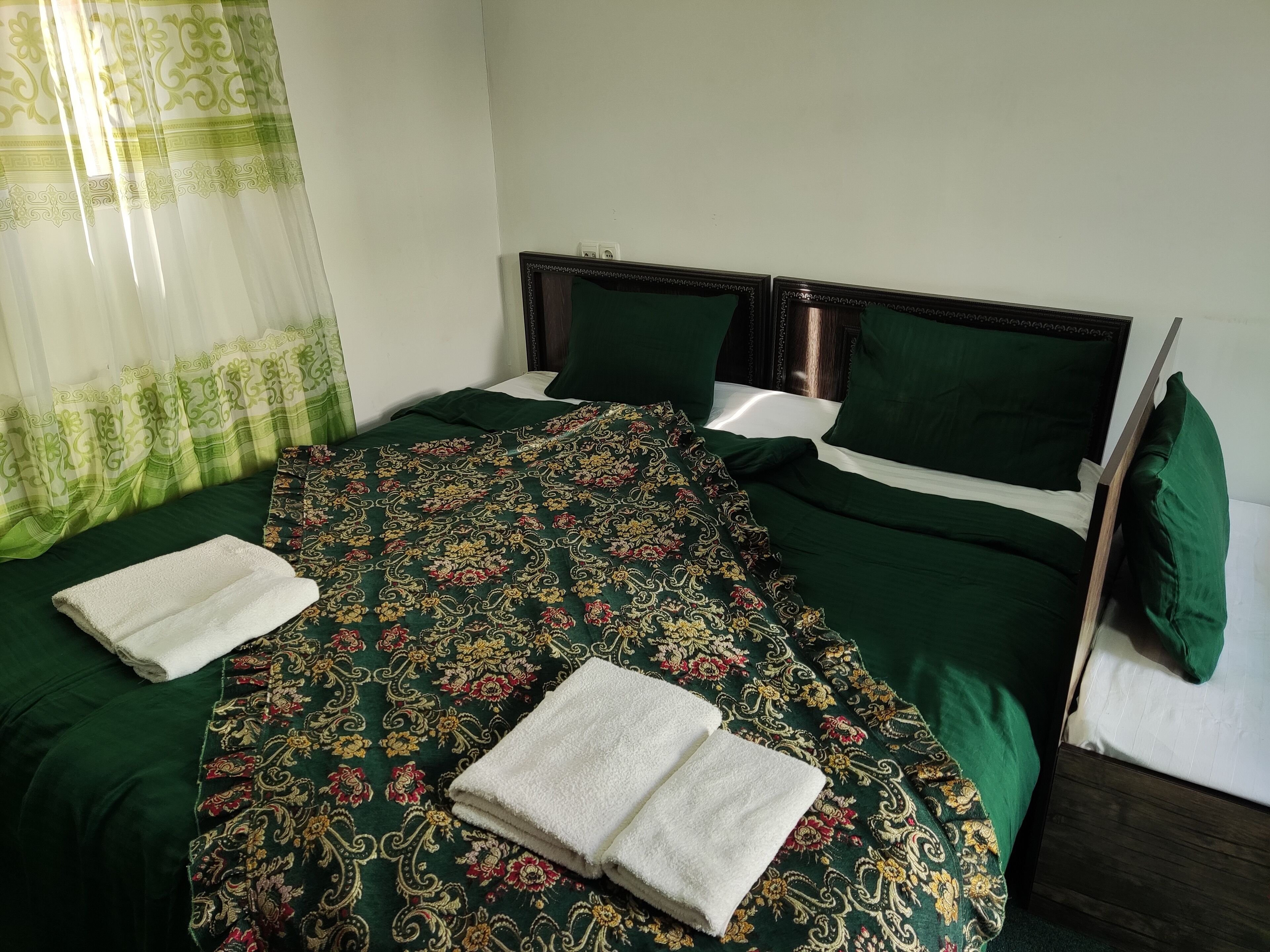 Quarto de hotel com uma cama grande, duas almofadas, um edredom verde e uma toalha branca.