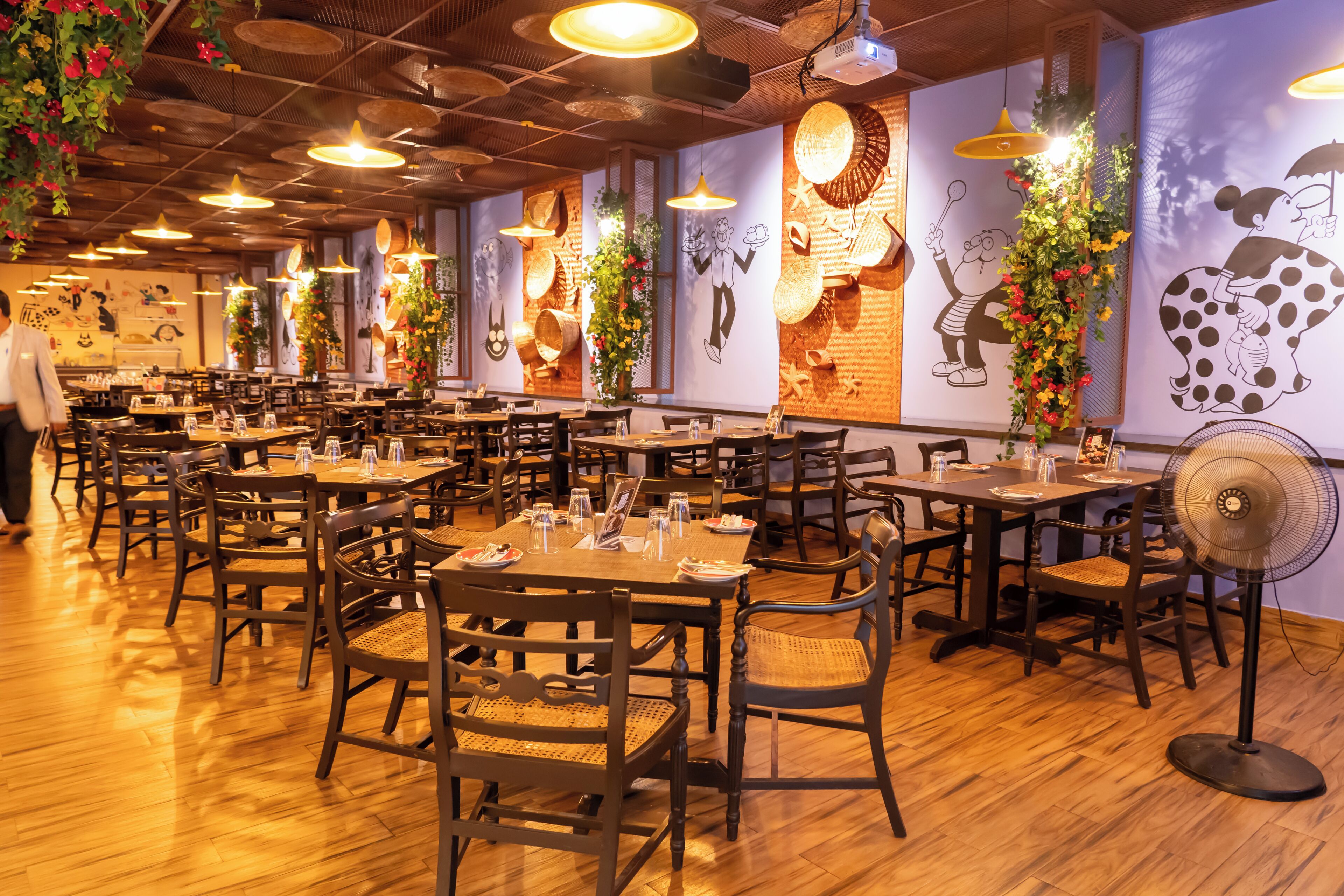 Um restaurante com mesas e cadeiras de madeira, luminárias pendentes e decoração na parede.
