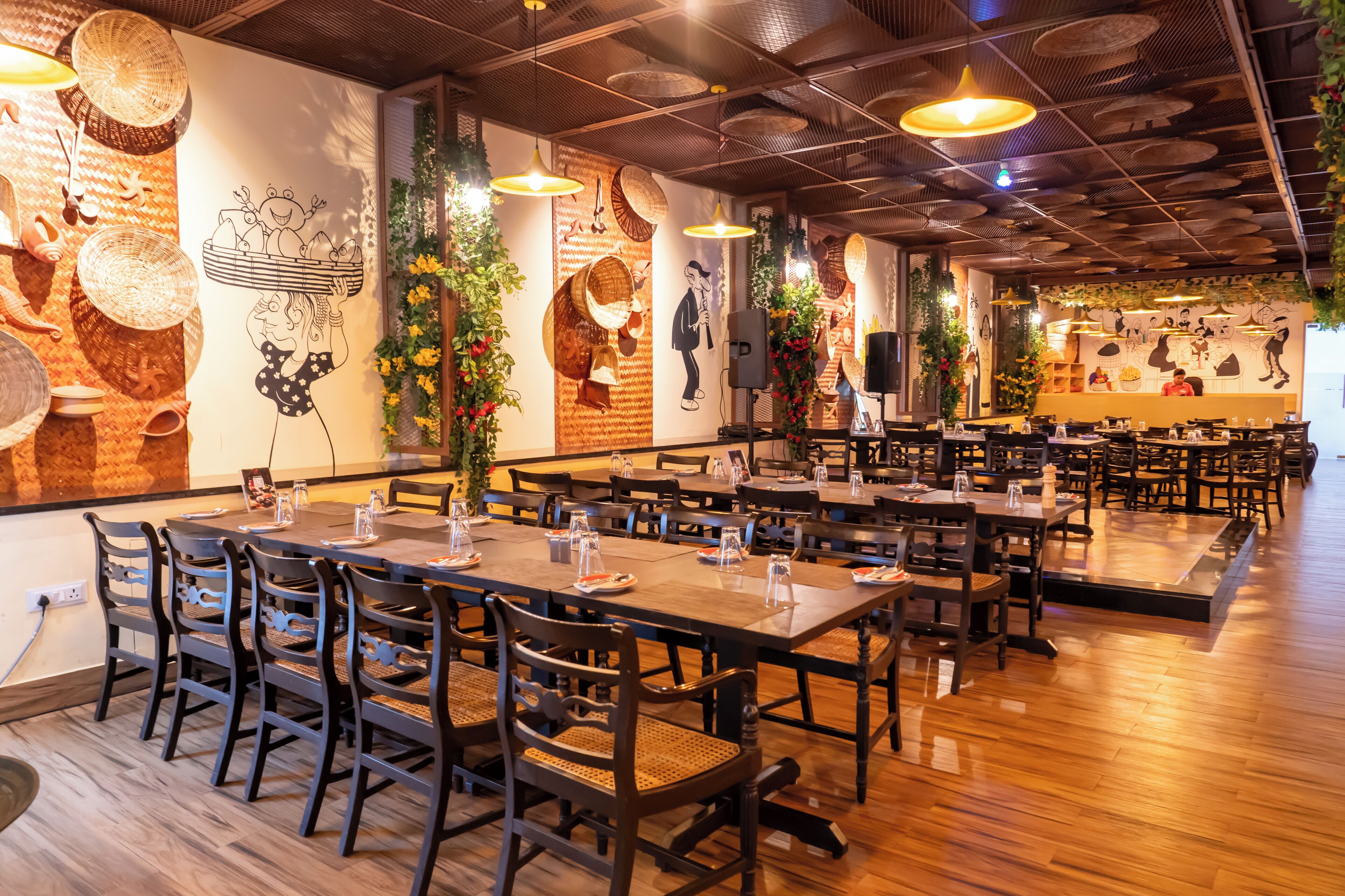Restaurante com várias mesas e cadeiras, teto alto com vigas aparentes e arte decorativa nas paredes.
