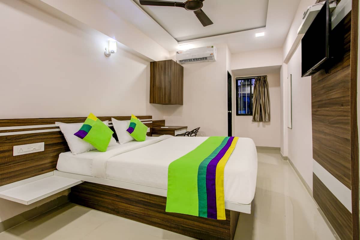 Quarto moderno com cabeceira de madeira, cama com manta colorida, mesa de cabeceira, televisão montada na parede e ar condicionado.