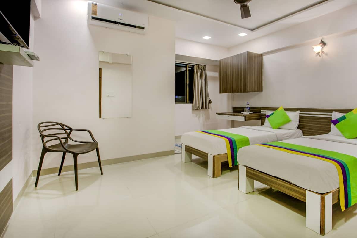 Quarto de hotel com duas camas, uma cadeira, uma mesinha e um espelho.