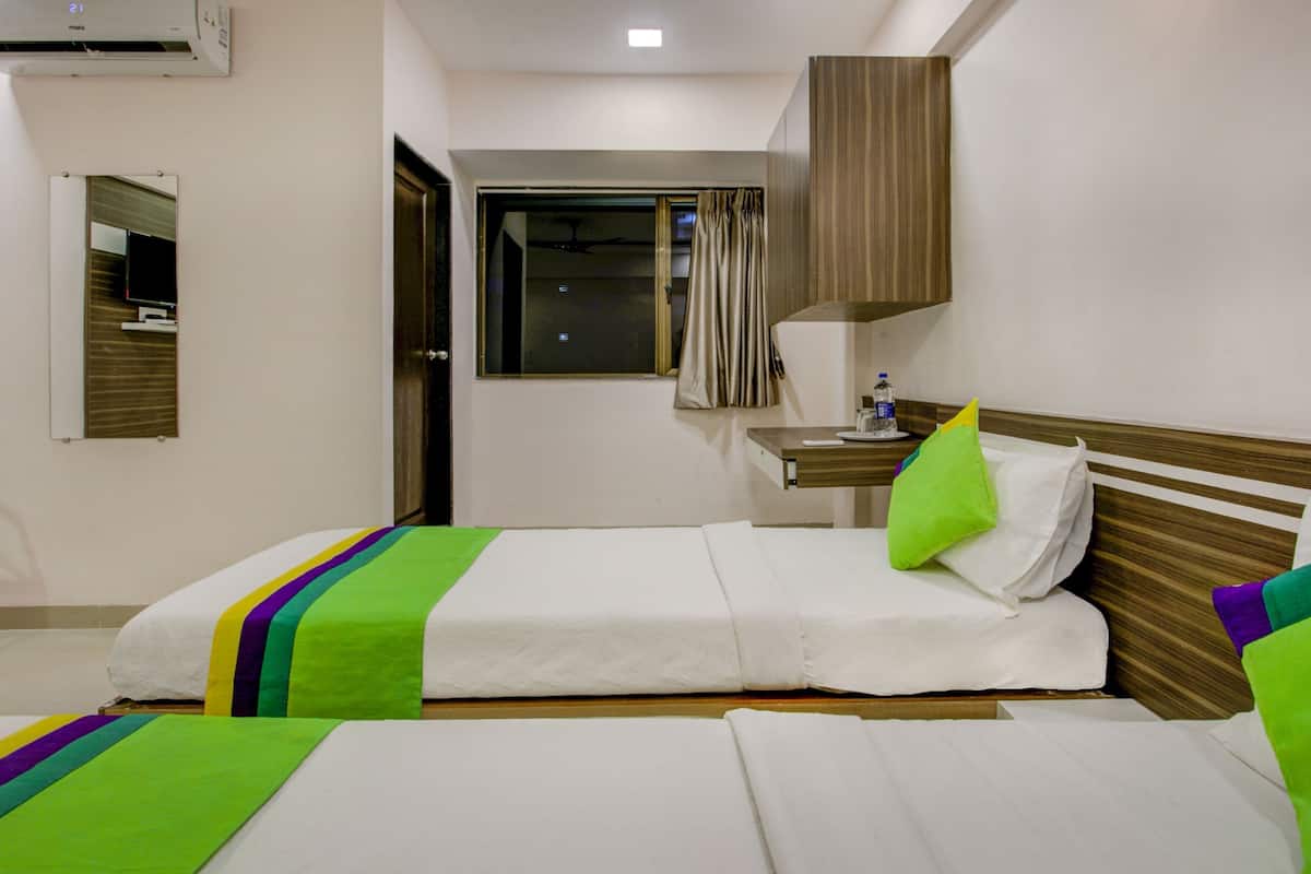 Quarto de hotel com duas camas, uma mesa de cabeceira, um espelho e uma janela com cortinas.