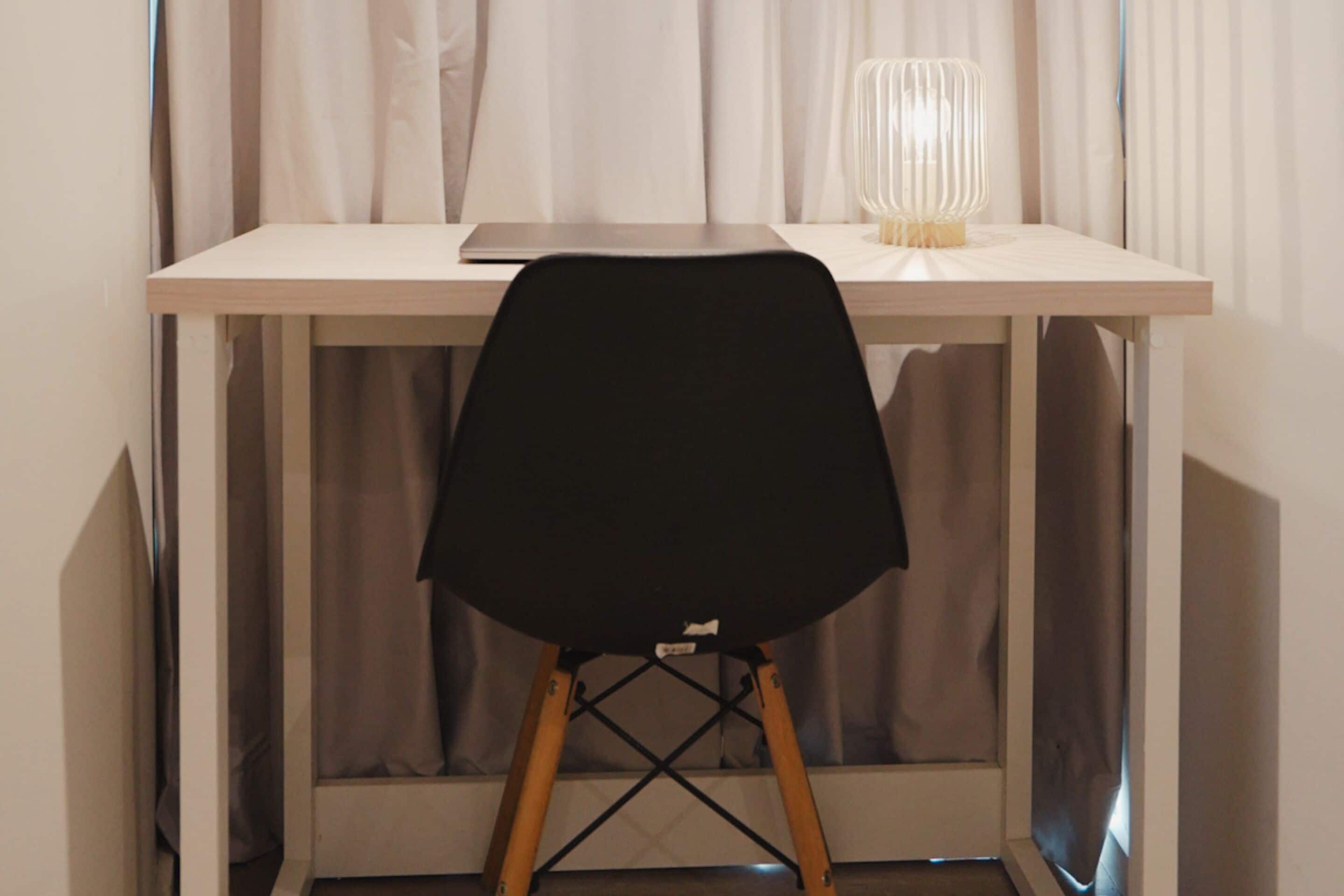 Uma mesa com um laptop, uma cadeira preta e um abajur branco.