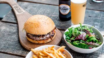 Uma refeição com hambúrguer, batatas fritas e salada sobre uma mesa de madeira.