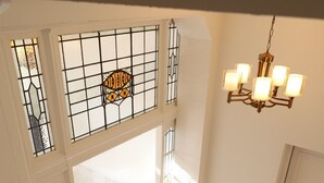 Uma escadaria com corrimão de madeira leva a um quarto com porta branca e um candelabro.