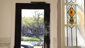 Uma porta com janela de vitrais, moldura preta e vista para uma rua residencial com casas e árvores.