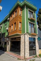Um edifício de vários andares com fachada verde, molduras de madeira nas janelas e base de pedra.