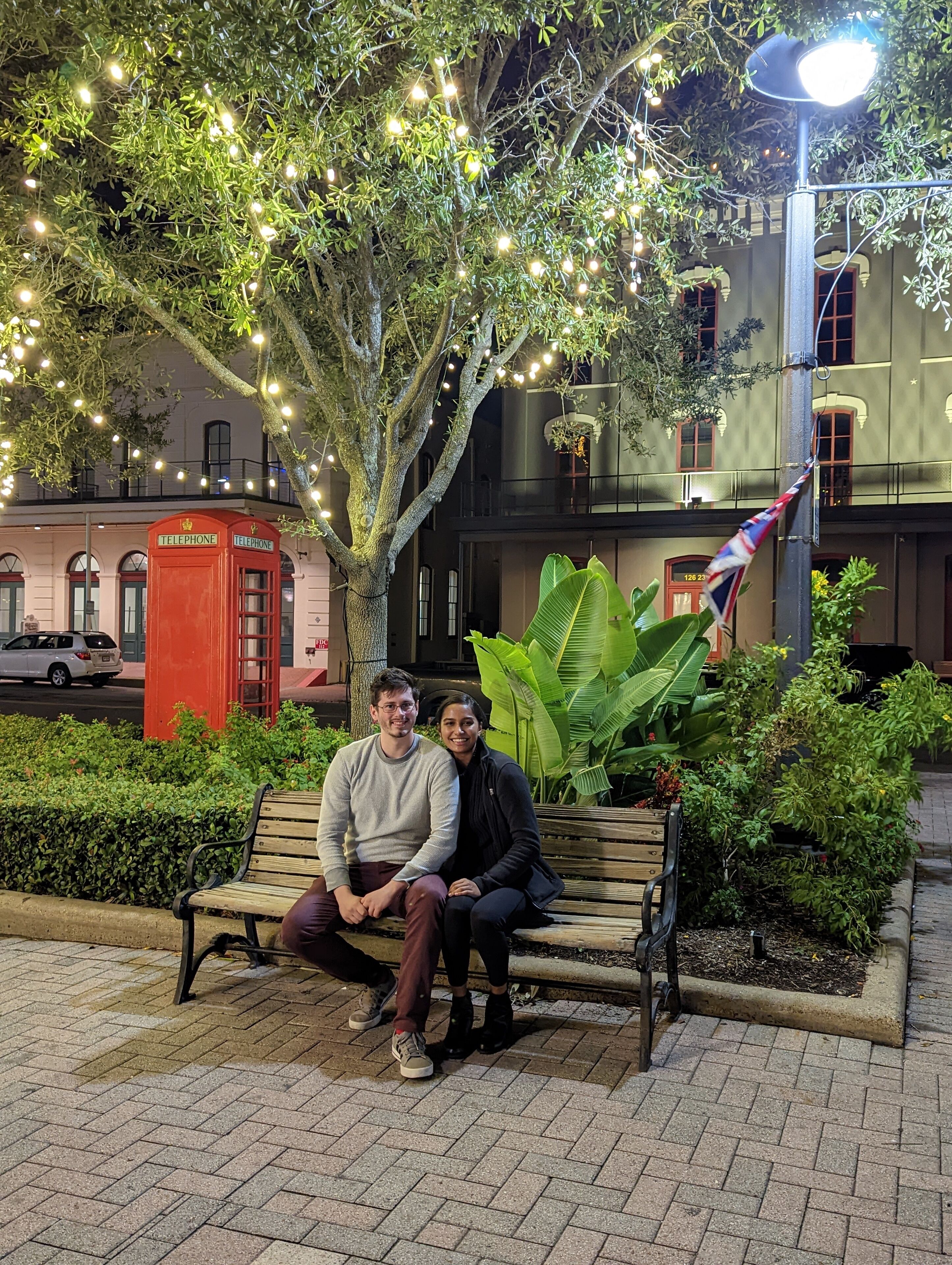Um banco numa área externa bem iluminada, com uma árvore e luzes de corda.
