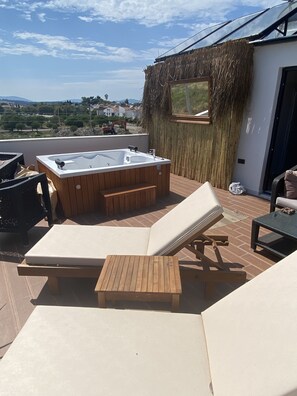 Terraço no telhado com banheira de hidromassagem, espreguiçadeiras e vista para a paisagem.